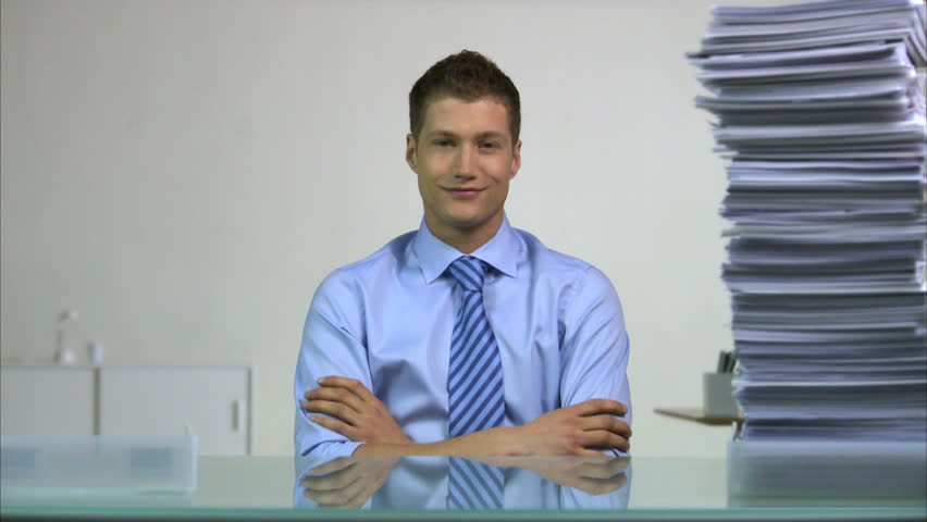 A Business Man Sitting Behind A Desk, Piles Of Paper Decreasing Stock ...