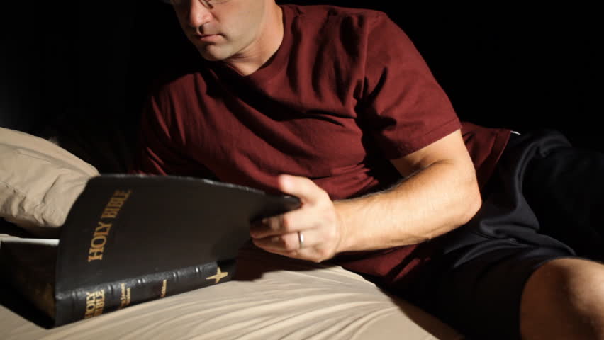 A Young Man Sitting In A Chair Reading From The Holy Bible. Green ...