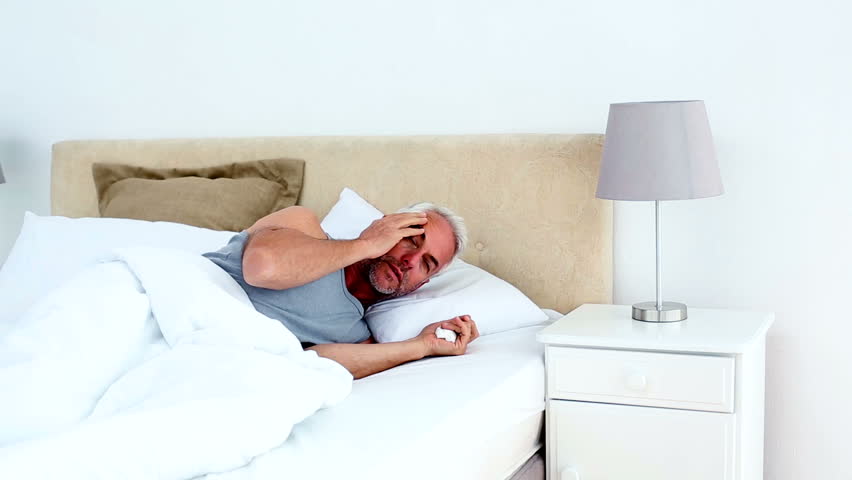 Groggy Man Waking Up And Looking At His Alarm Clock At Home In Bedroom ...