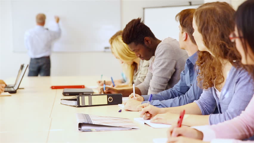 Students Writing In Classroom With Teacher Writing On Whiteboard (Full ...